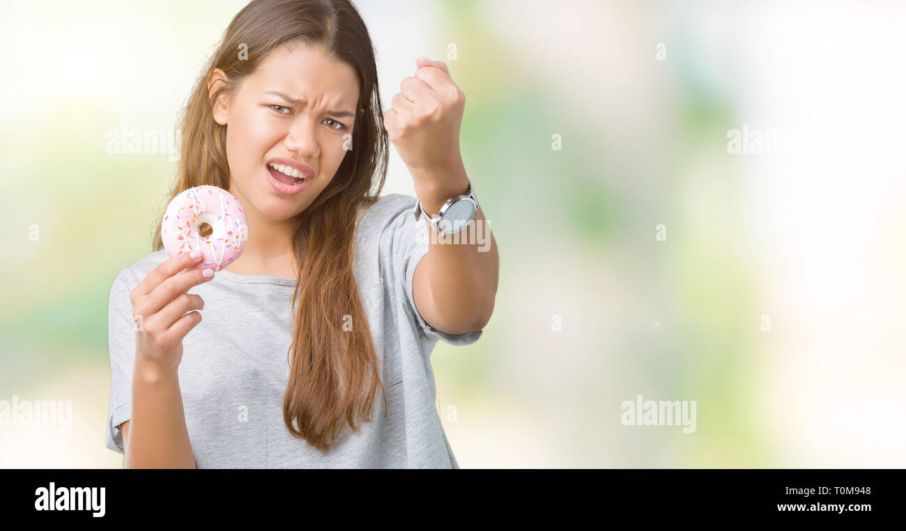 Young beautiful woman eating pink donut over isolated background ...