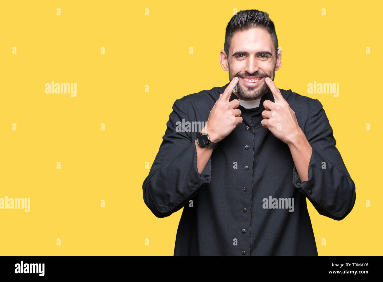 Young Christian priest over isolated background Smiling with open mouth ...