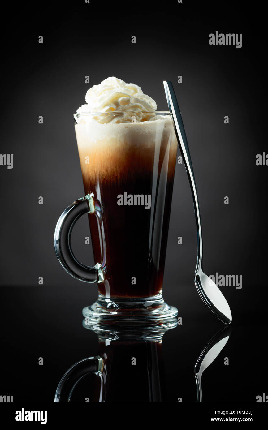 Layered coffee cocktail with whipped cream on a black reflective ...
