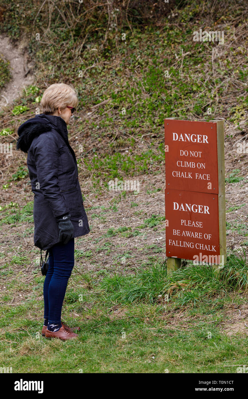 Woman reading a warning sign at the bottom of a chalk escarpment in ...