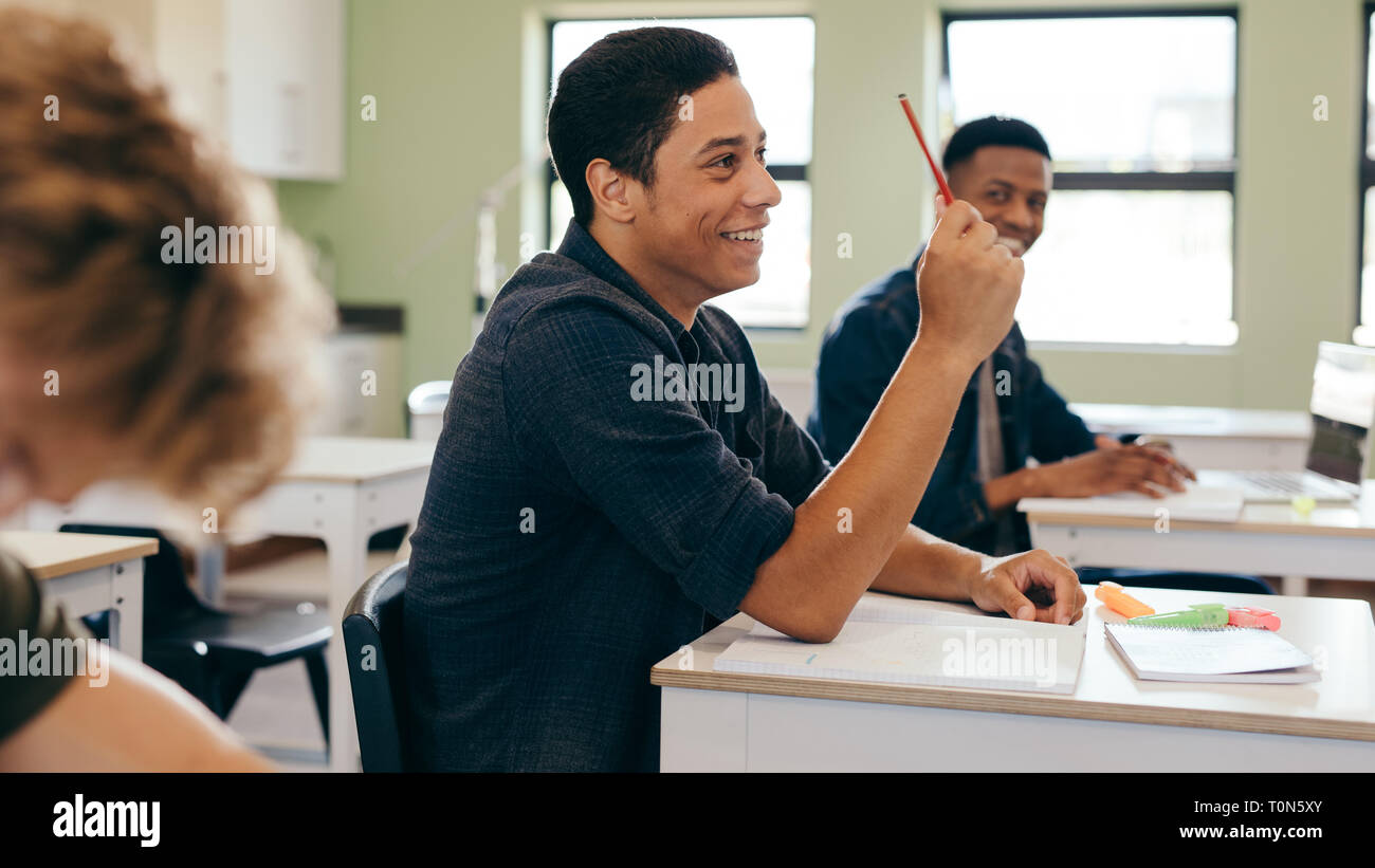 Male student sitting in the class and raising hand up to ask question during lecture. High ...