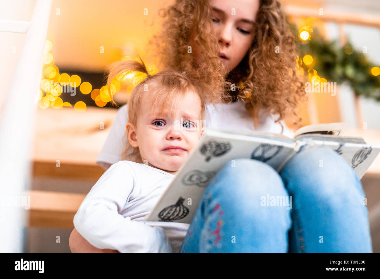 Elder sister reading book aloud to her younger sister at staircase ...