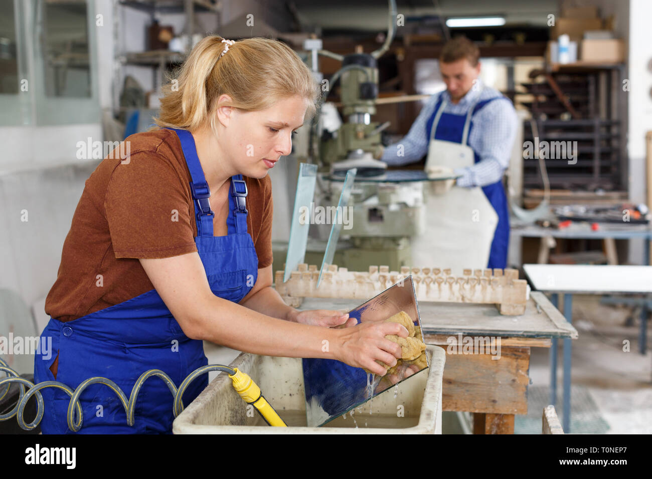 Experienced female worker cleaning cut glass in industrial workshop ...