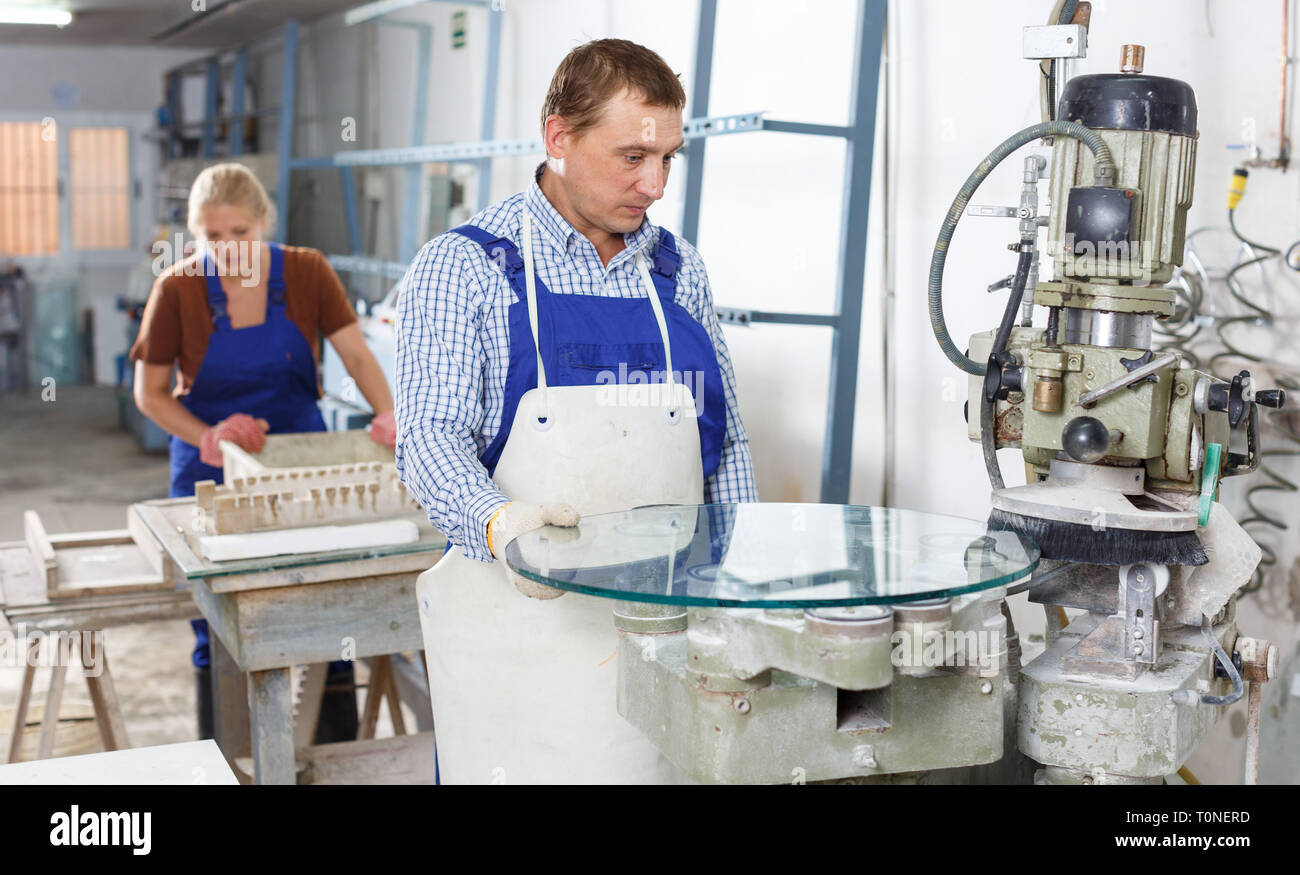 Confident male glazier with female assistant working on curved glass ...