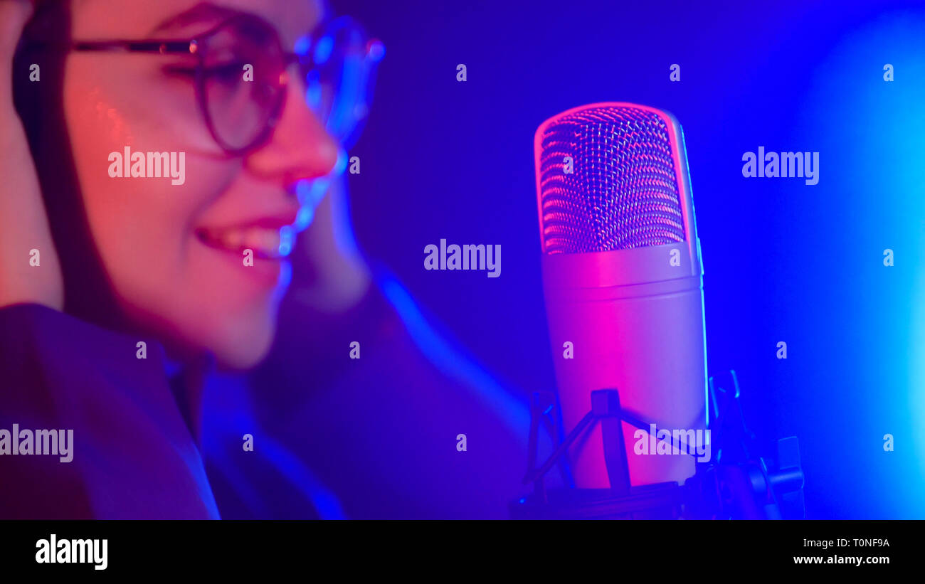 A young smiling woman in glasses singing in neon lighting by the ...