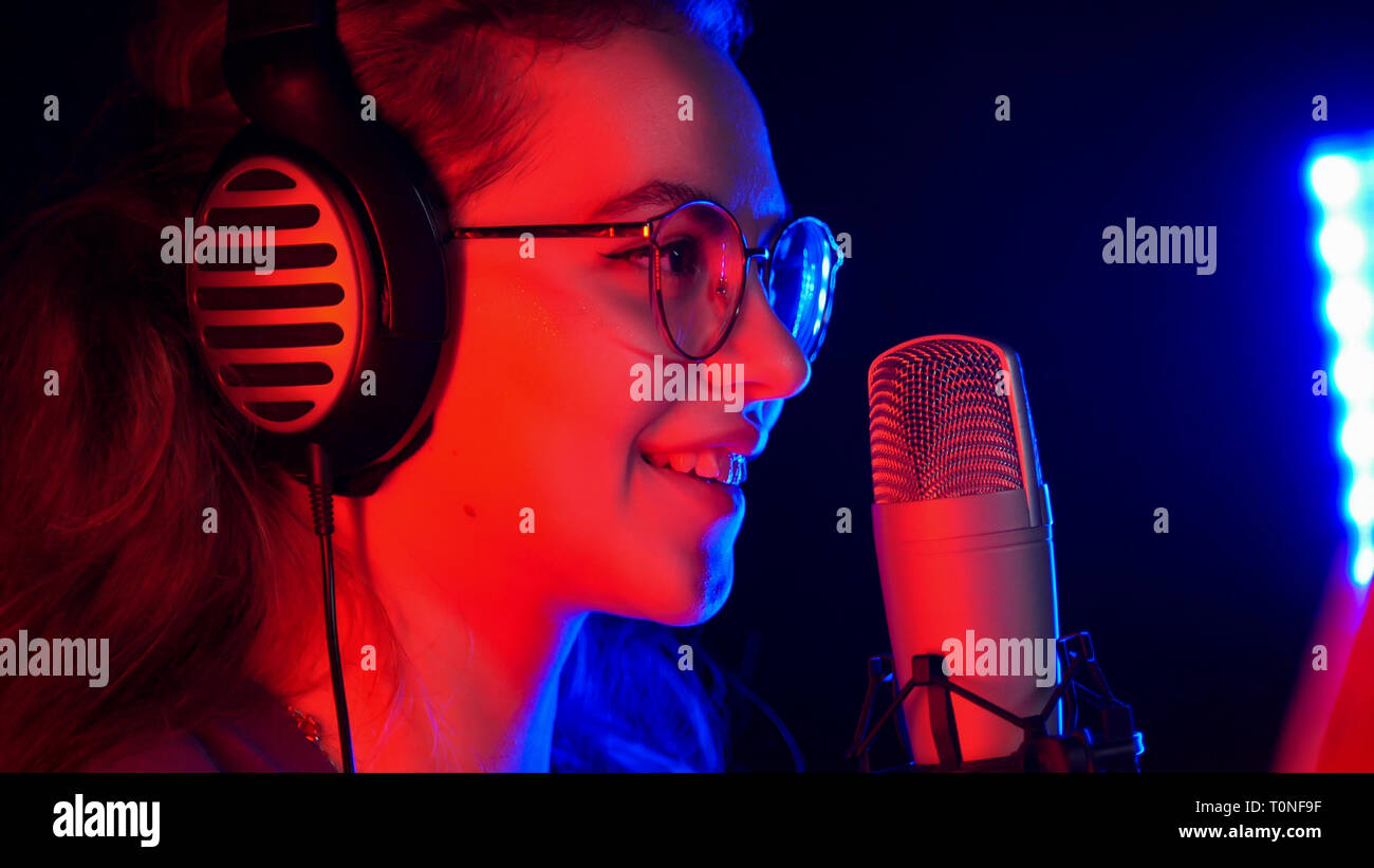 A young smiling woman in glasses singing by the microphone in neon ...