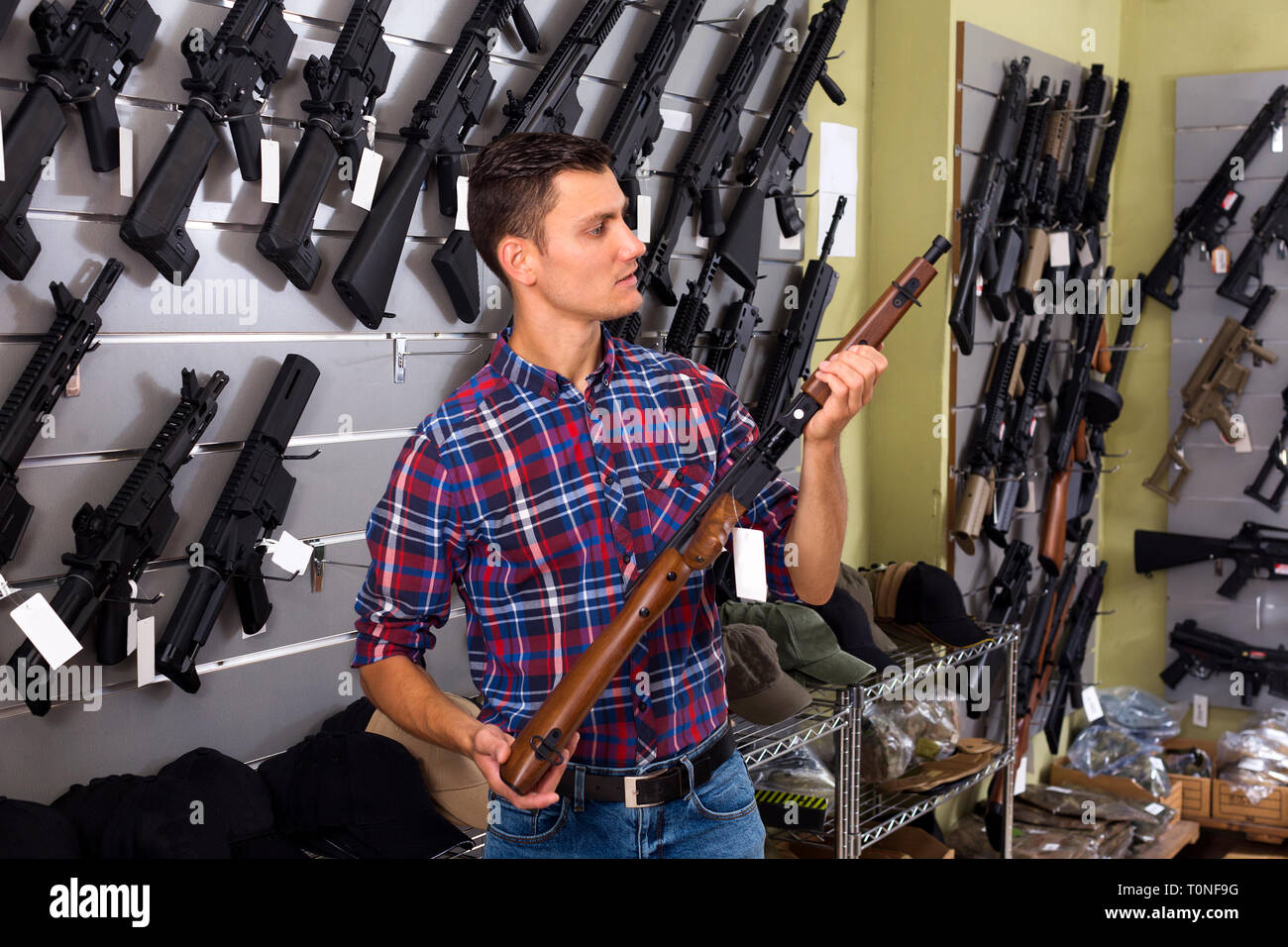 Happy young guy choosing air rifle in military store Stock Photo - Alamy