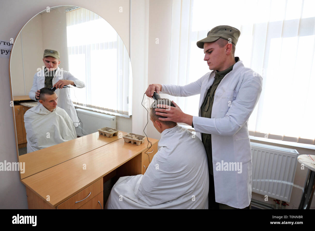 At the utility room. Army barber cutting soldier’s hair with a ...