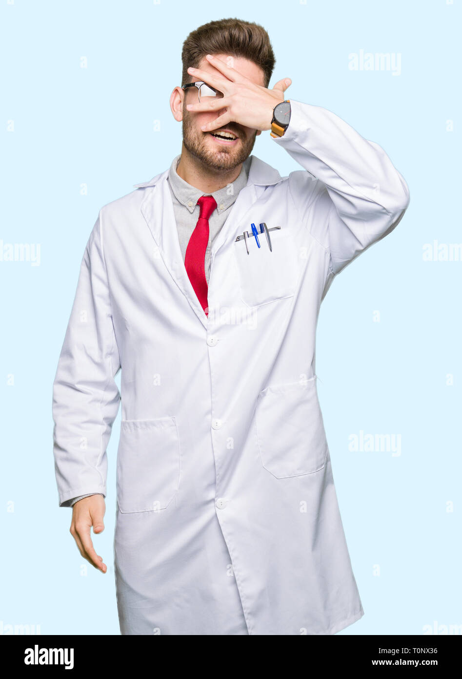 Young handsome scientist man wearing glasses peeking in shock covering ...