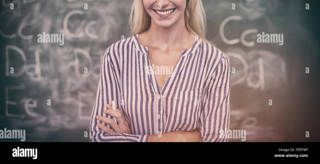 Portrait Of Happy Teacher Standing With Arms Crossed In Classroom Stock