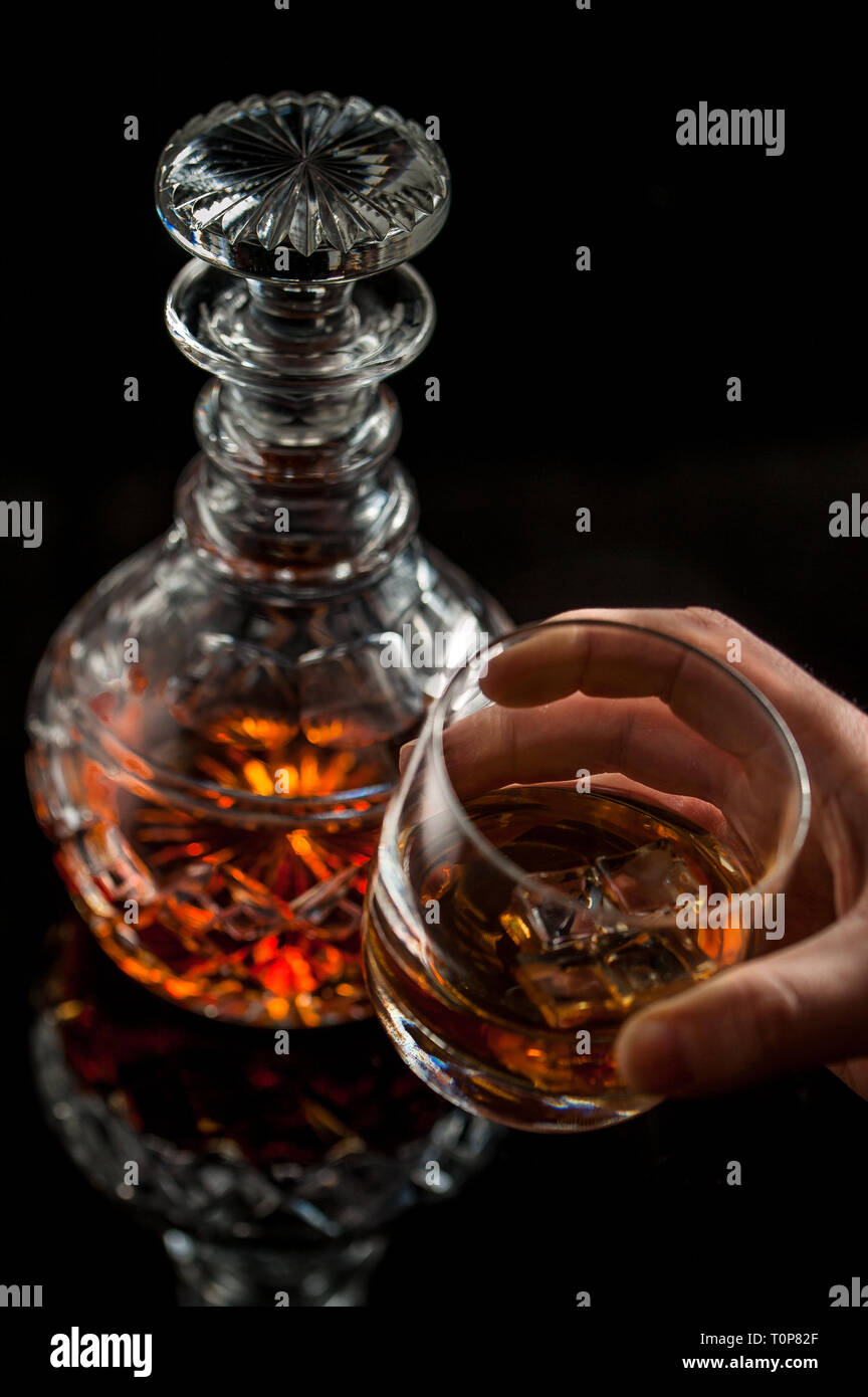 Whiskey glass hold by man hand and crystal decanter on dark background ...