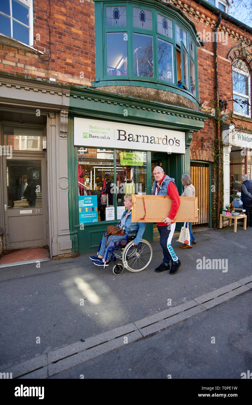 A disabled person using a wheelchair outside of a Barnardo's shop, on a ...