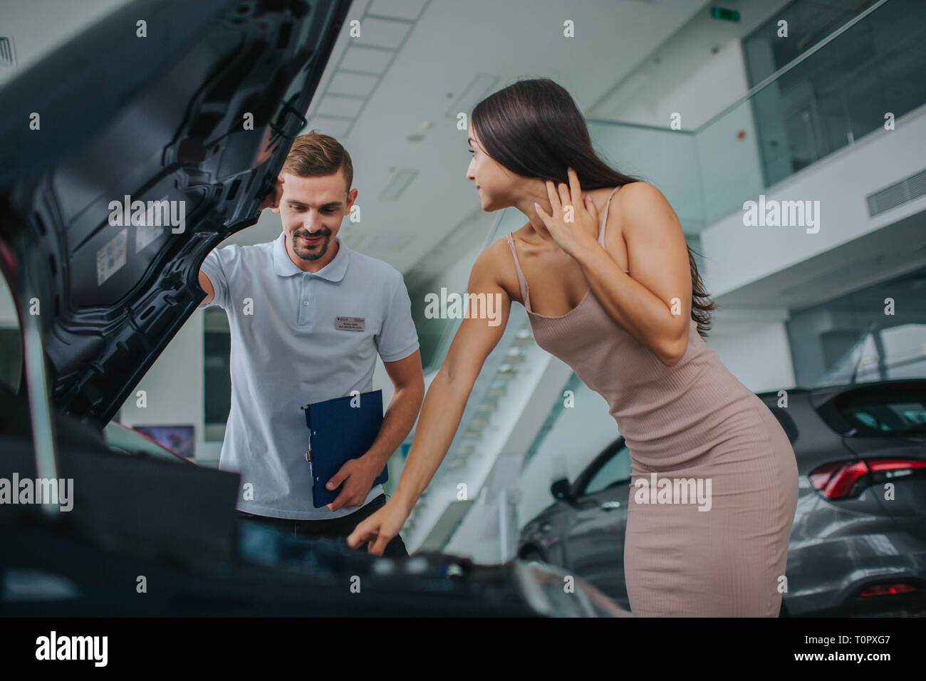 Well-built and nice brunette stands at opened body of car and leans on ...