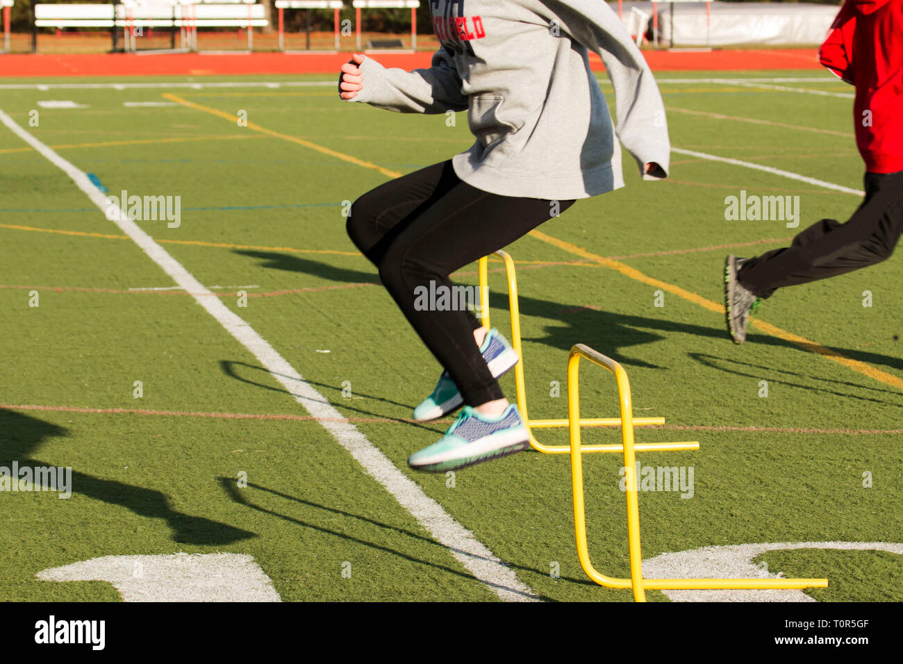 An athlete at track and field practice jumps over yellow hurdles on a green turf field Stock ...