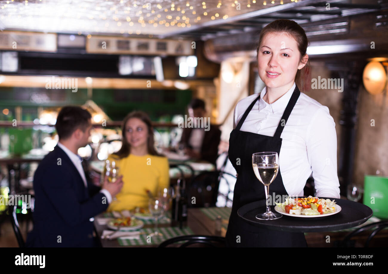 Portrait of female waiter who is holding tray with order in hall of ...
