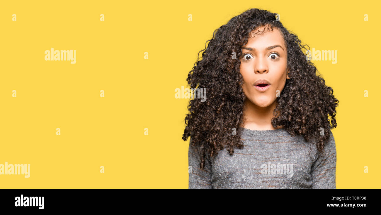 Young beautiful woman with curly hair wearing grey sweater afraid and ...
