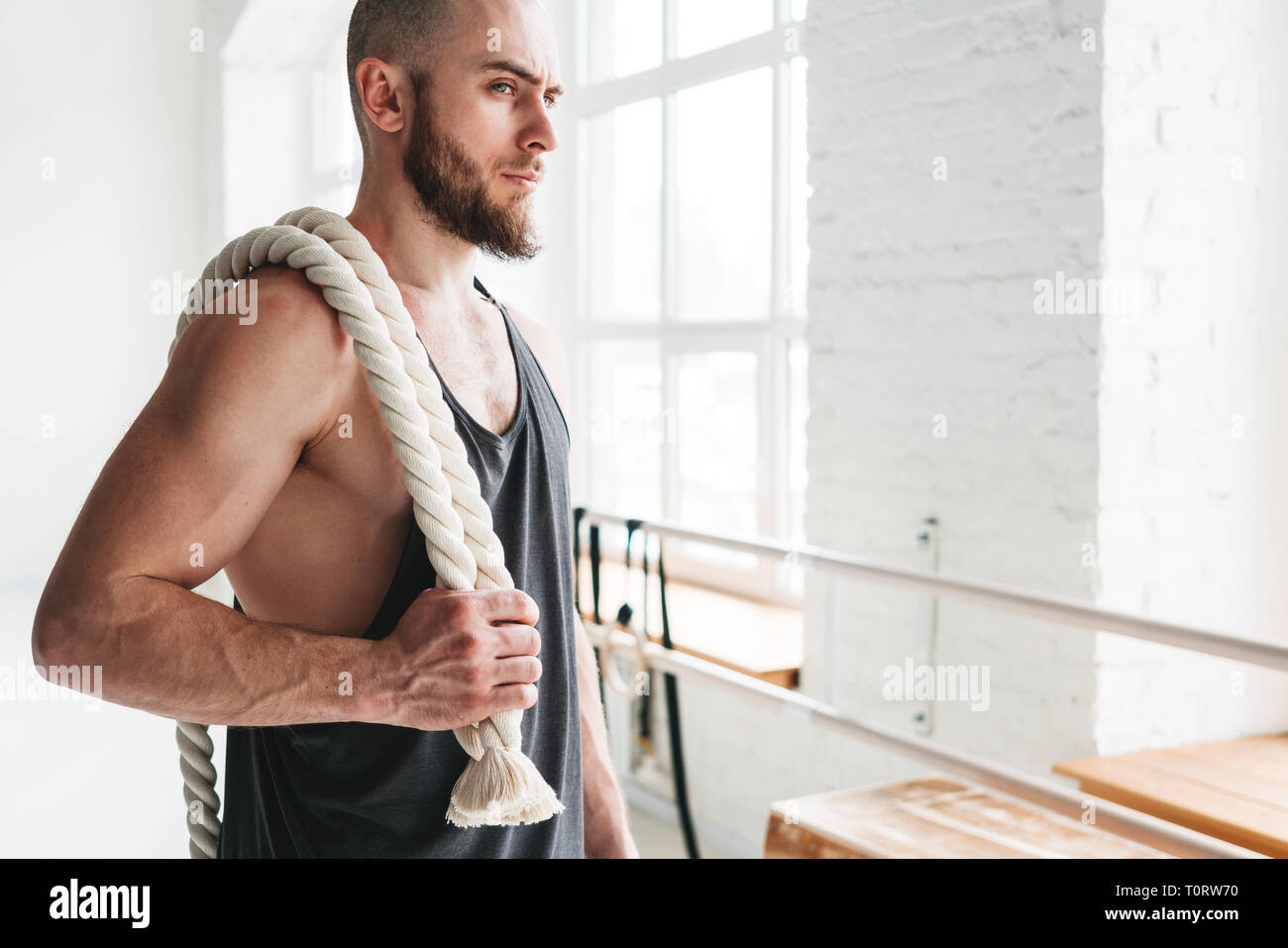 Handsome muscular man holding on shoulder rope workout in light gym ...