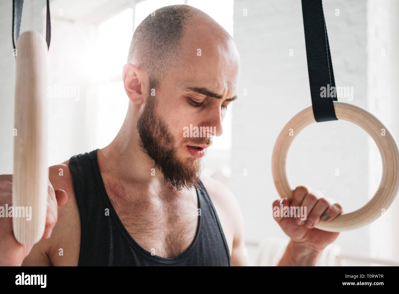 Tired handsome strong man holding on to gymnastic rings at cross gym ...