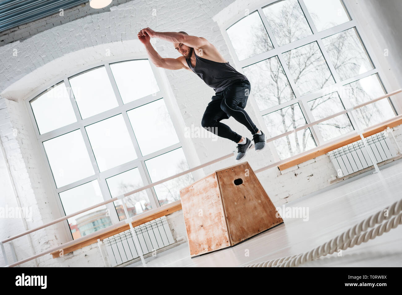 Dynamic shot of fitness male athlete jumping at square box in cross gym ...