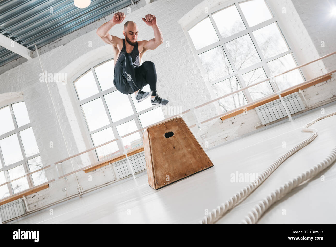 Dynamic shot of fitness male athlete jumping through at square box in ...