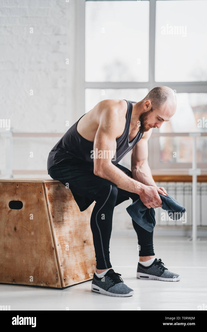 Muscular man sitting on box at gym. Male athlete relaxing after his ...