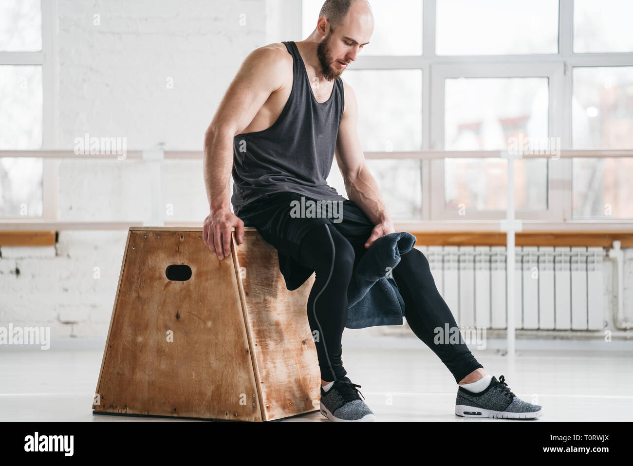 Tired strong man sitting on box at gym. Perspiring fit sportsman ...