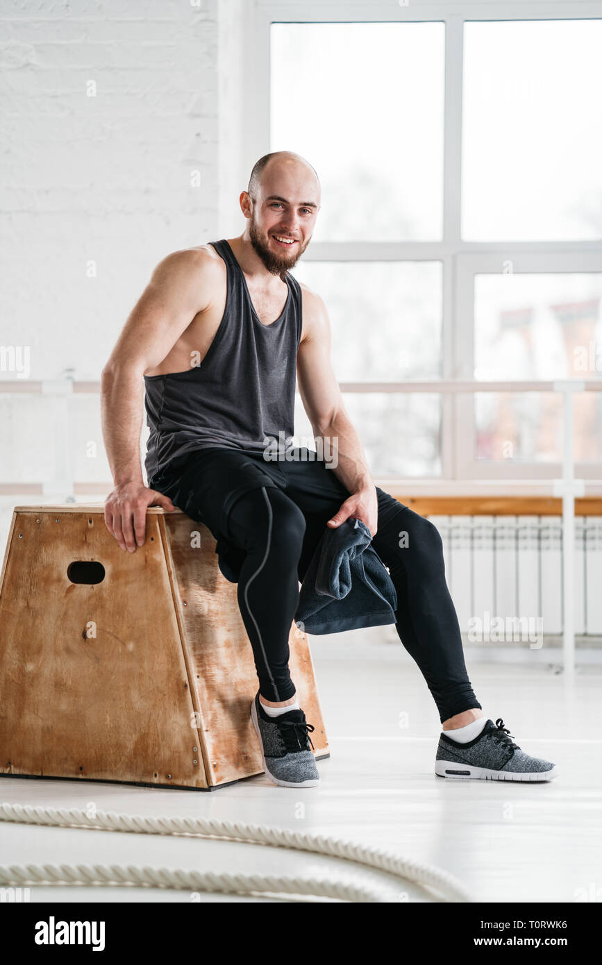 Smiling male athlete sitting at box in gym. Strong fit man resting ...