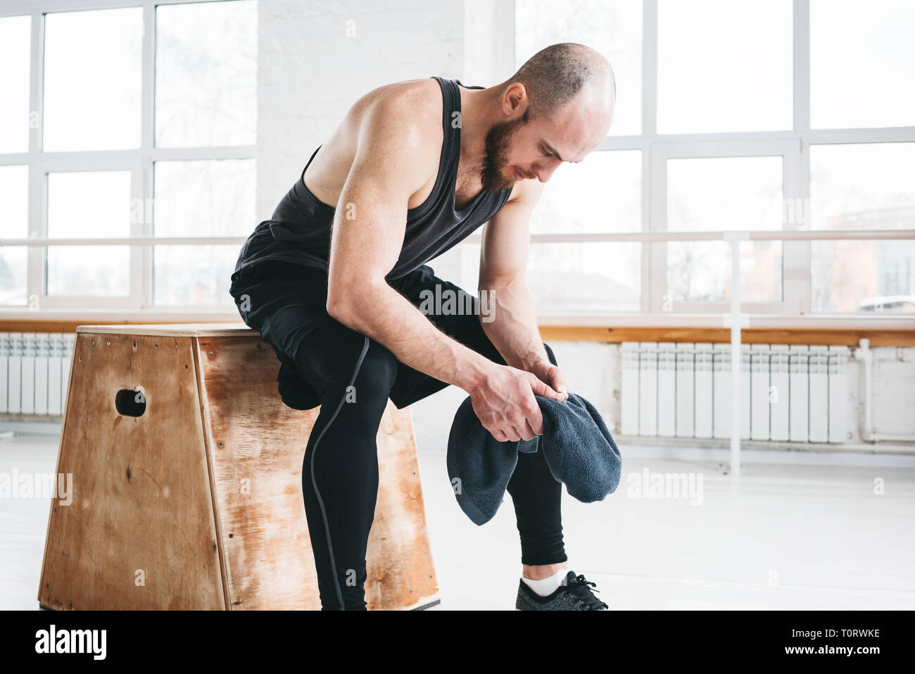 Tired muscular man sitting on box in cross gym. Strong male athlete ...
