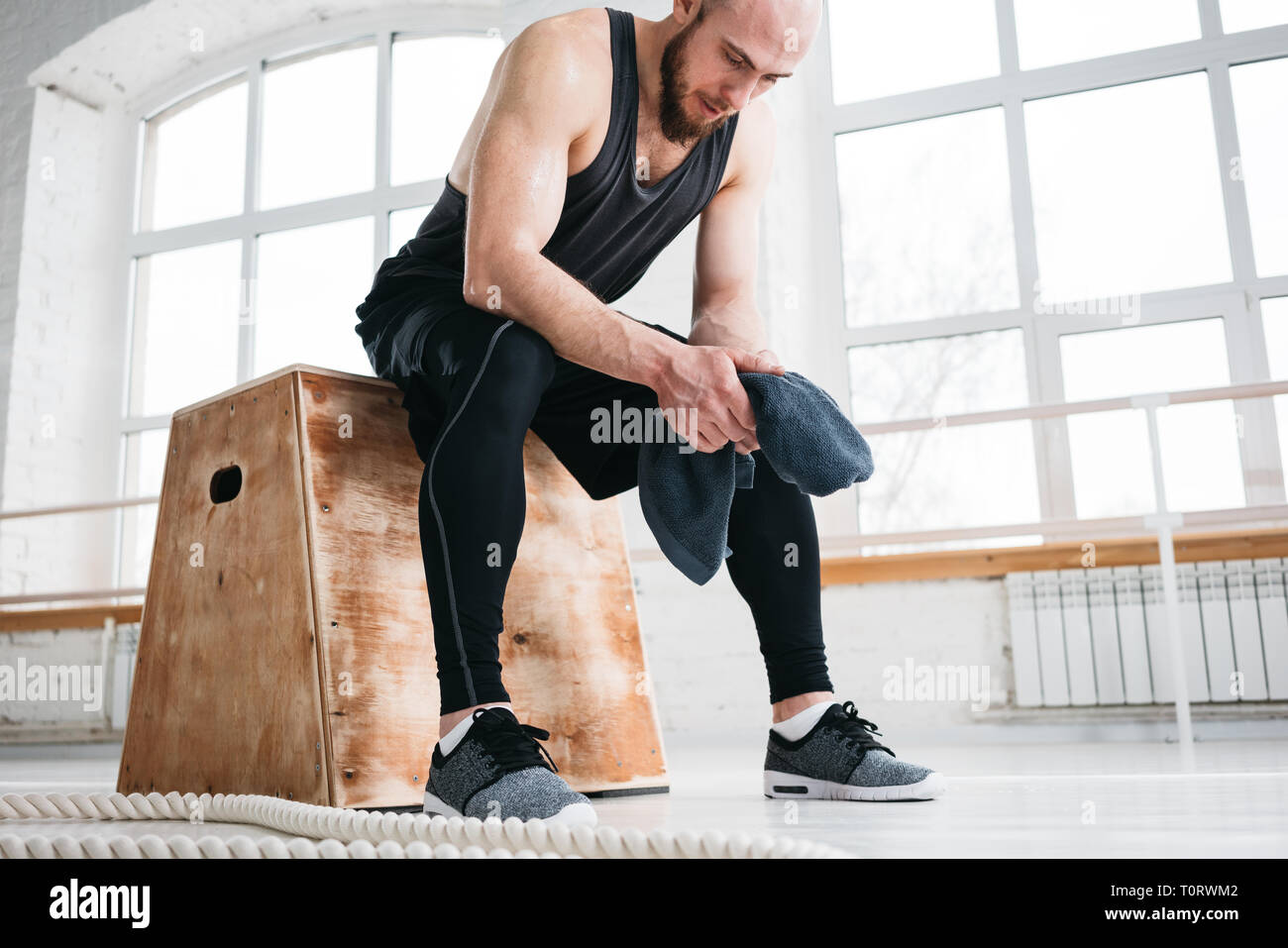 Tired strong man sitting on box at gym. Perspiring fit sportsman ...