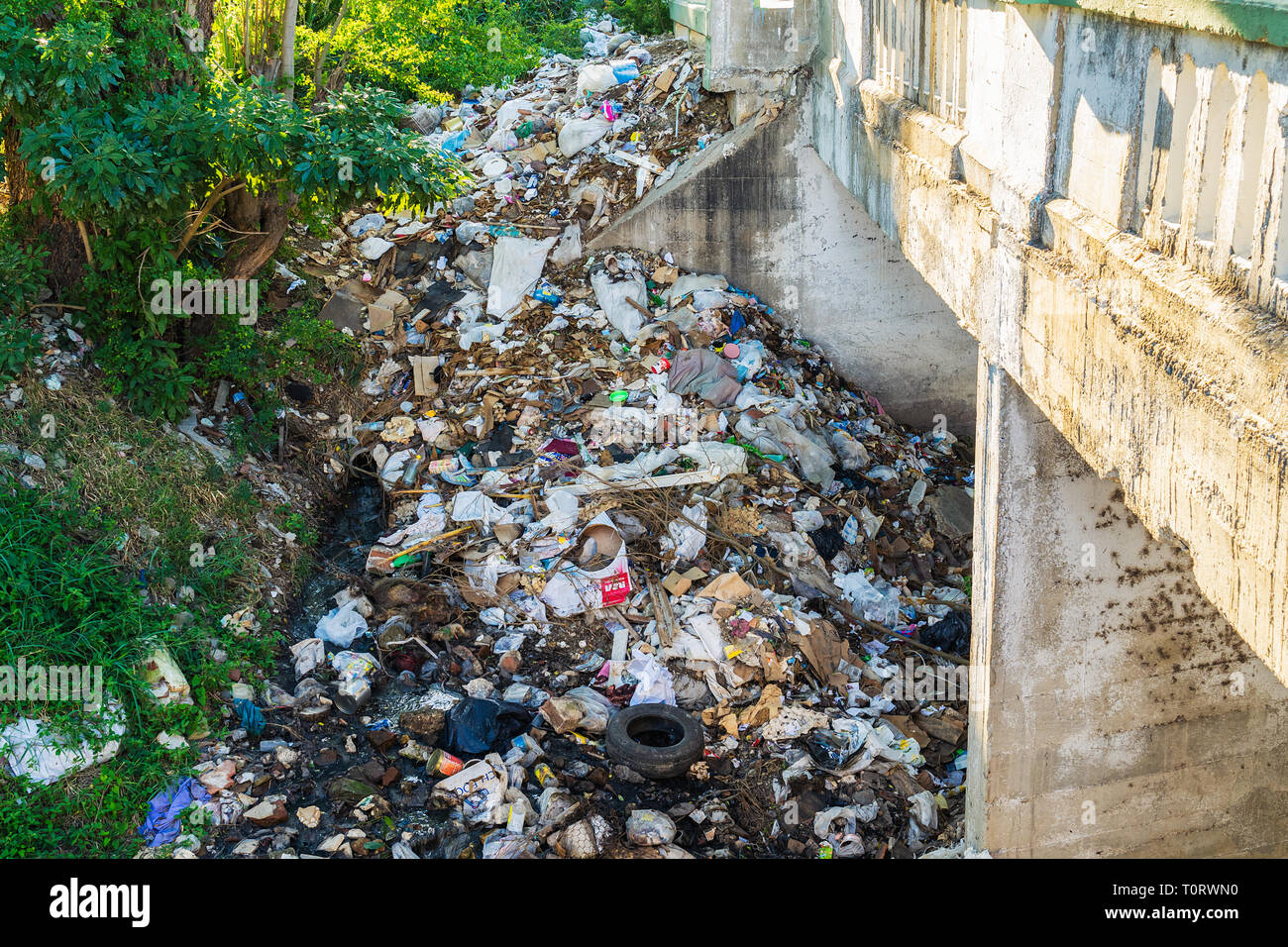 Garbage waste on the side of a river under a bridge Stock Photo - Alamy