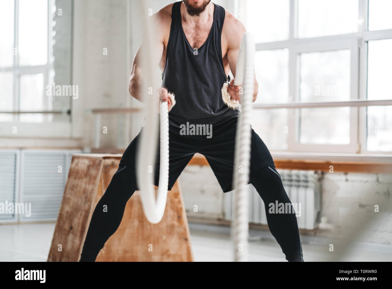 Fit man working out with battle ropes at hall. Male athlete training ...