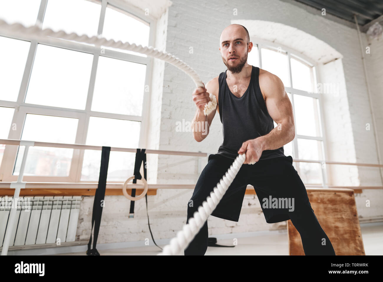 Strong man workout with battle ropes at light gym. Muscular sportsman ...