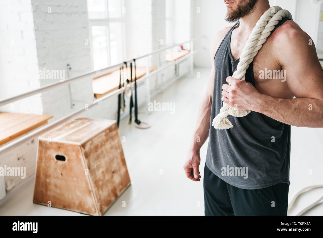 Handsome muscular man holding on shoulder rope workout in light gym ...