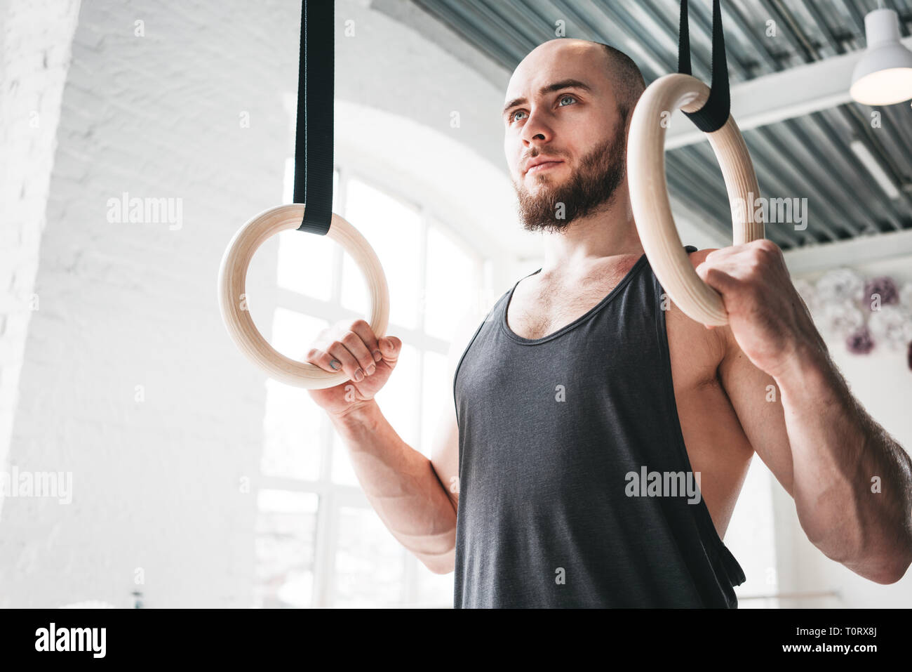 Male athlete holding gymnastic rings at gym. Fitness man is hanging on ...
