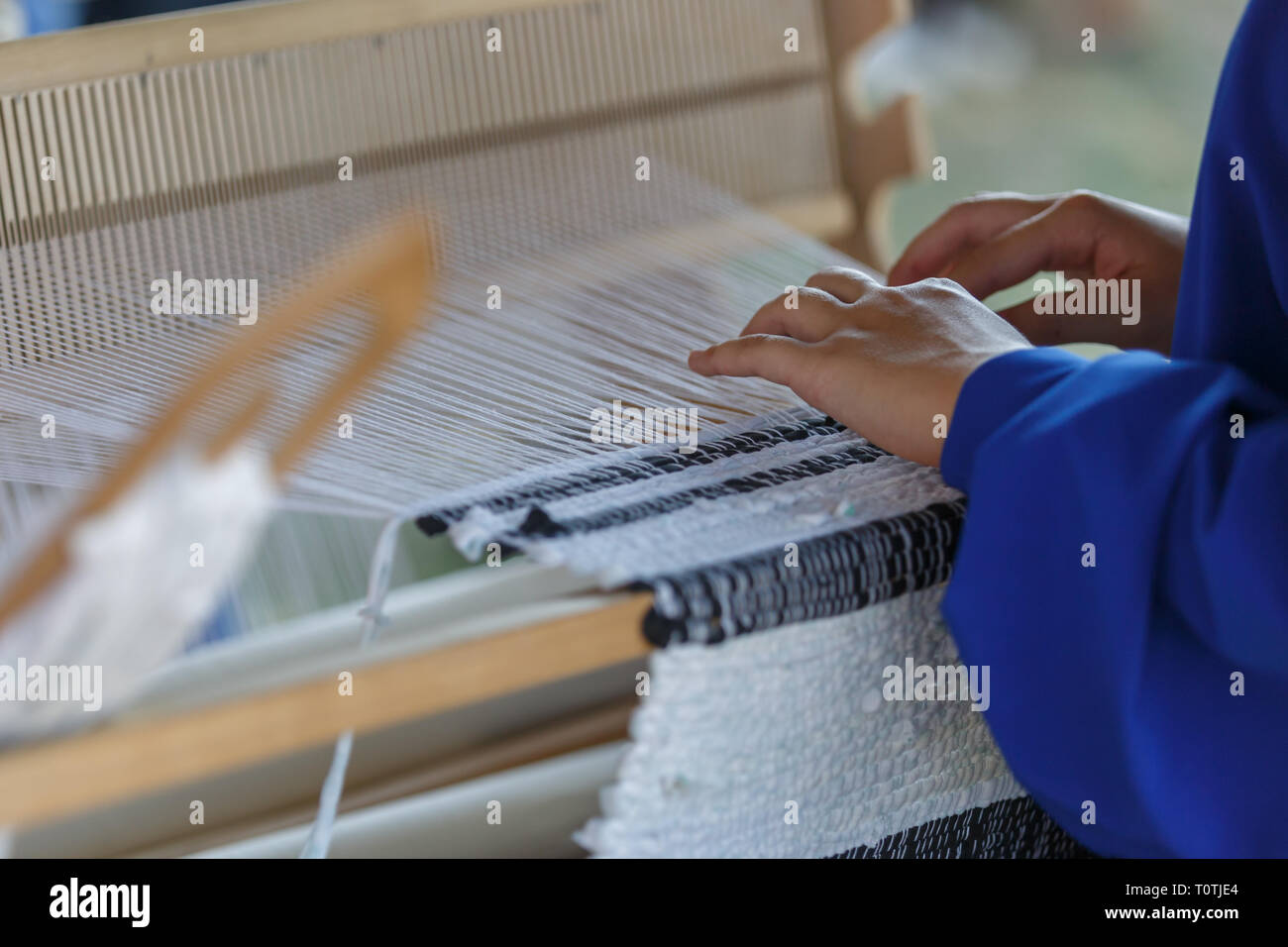 Young woman weaves a white cloth on a hand wood loom. Traditional ...