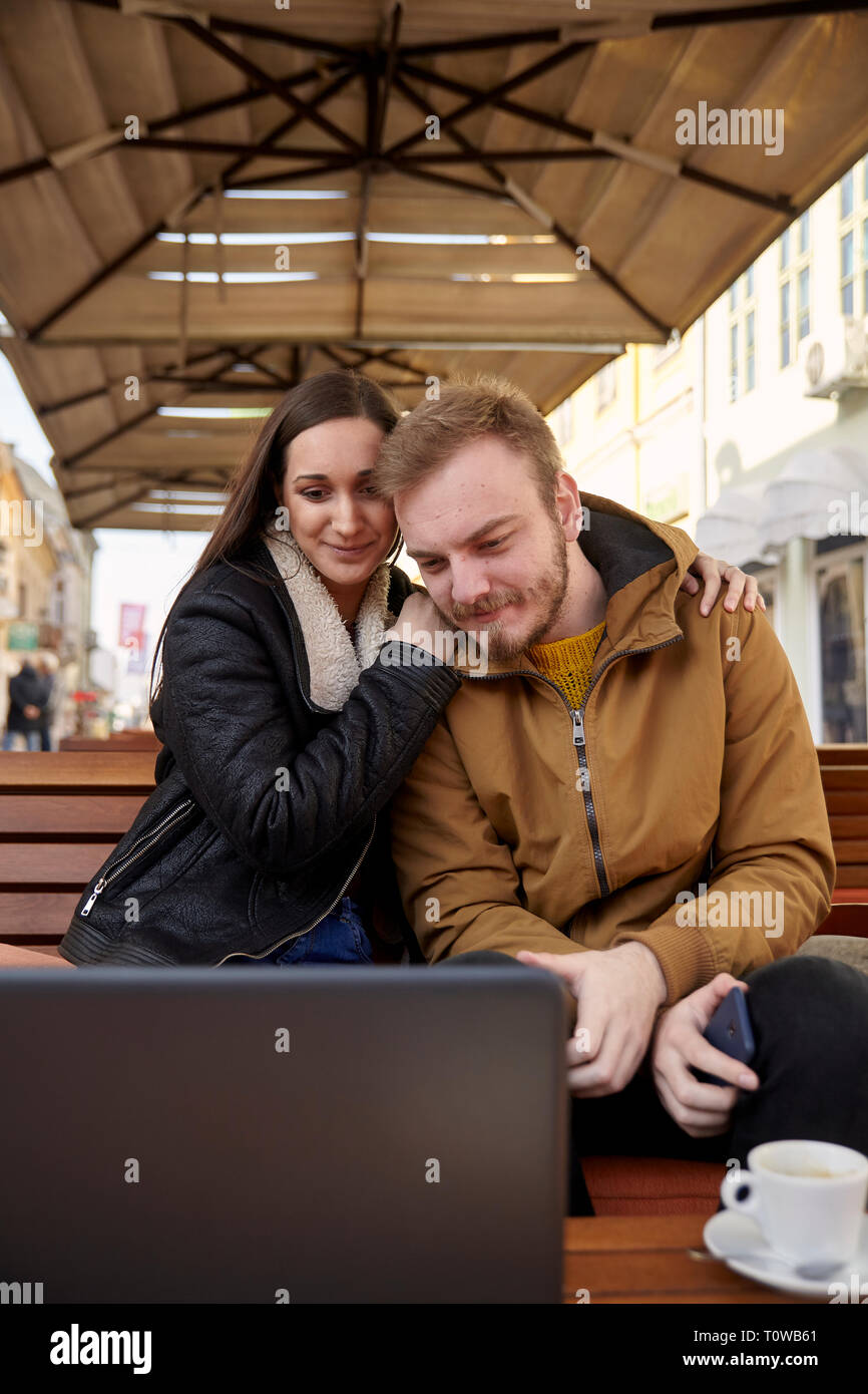 two people hugging couple, looking at a laptop computer in a cafe Stock ...