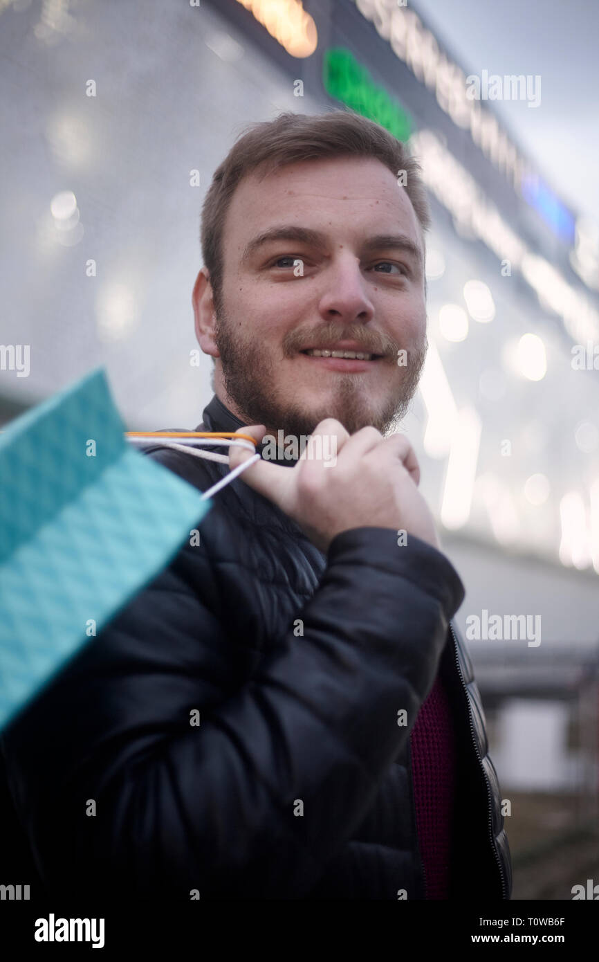 face, head portrait of young man holding shopping bags in front of a ...