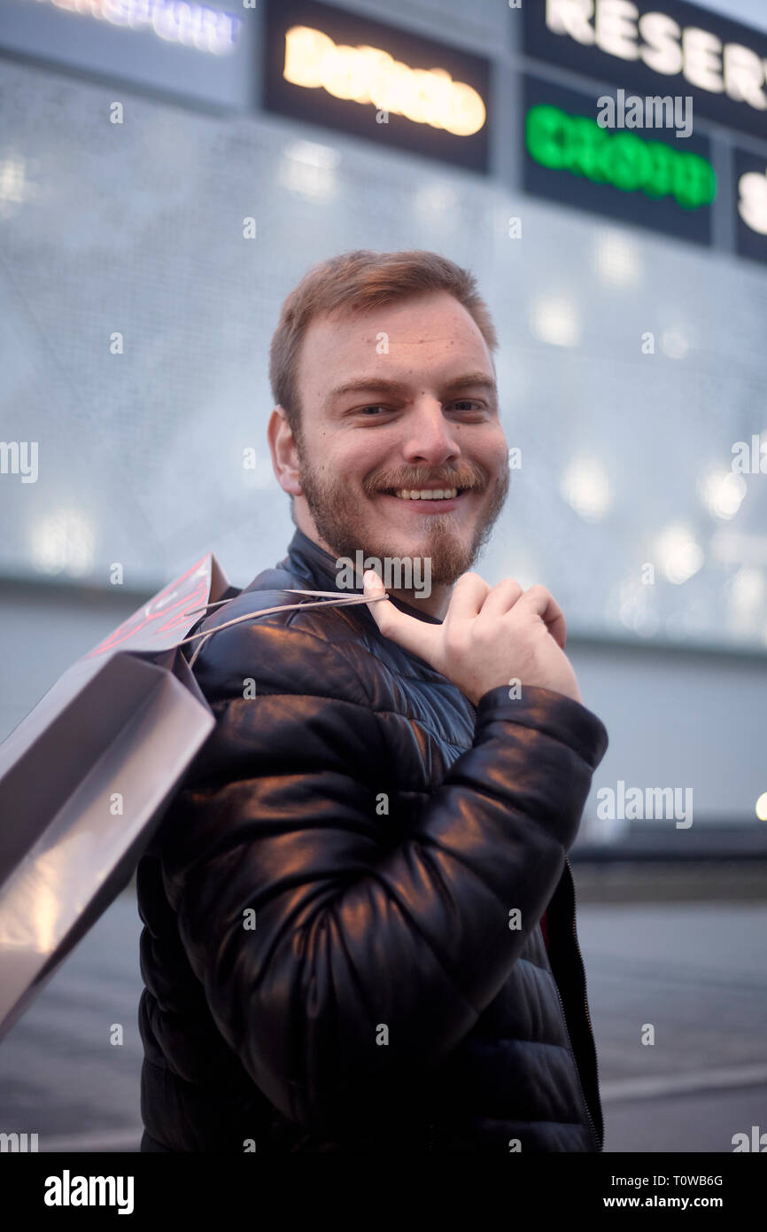 one young smiling man, looking to camera in front of a shopping mall ...