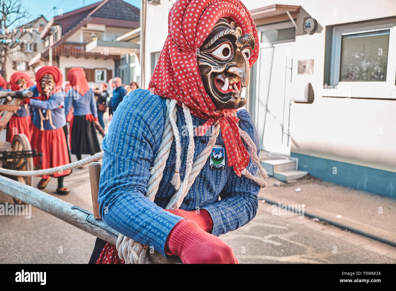 Pretty witch pulls a wooden plank. Street Carnival in Southern Germany ...