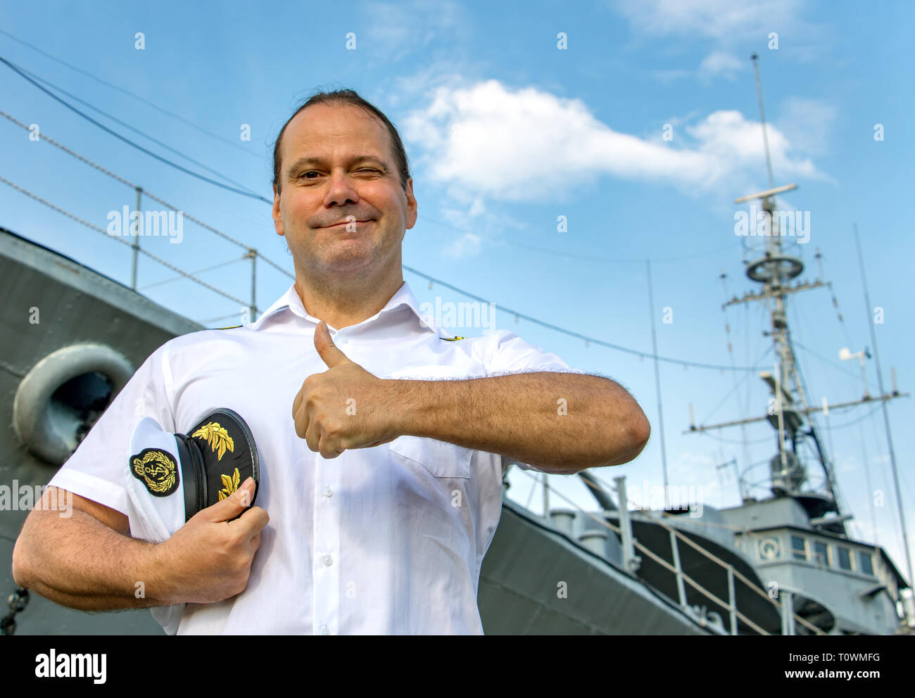 Captain standing in dock before warship and shows thumb up. A sailor ...