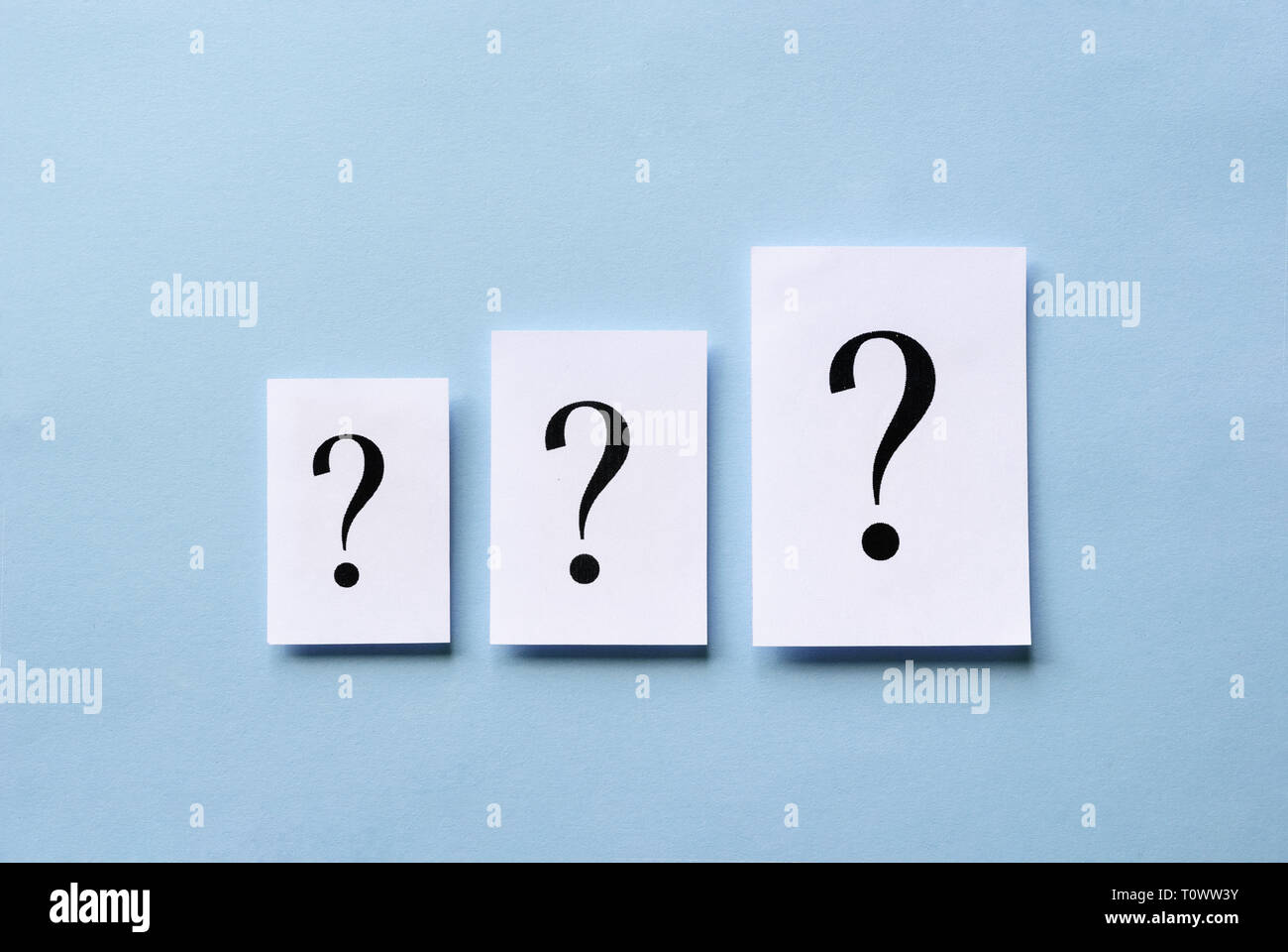 Three question marks of different size printed on white cards arranged ...
