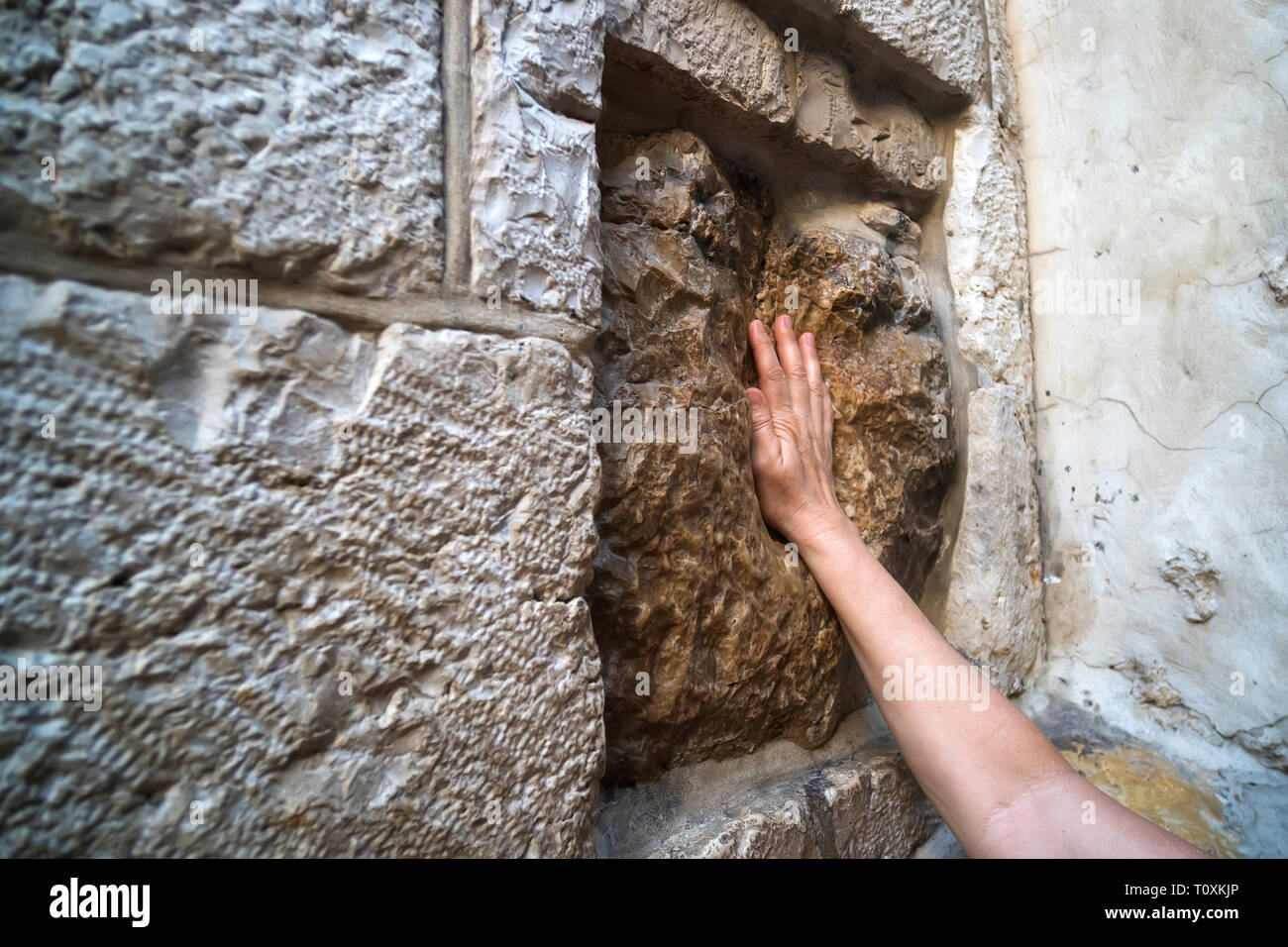 Close up of young man's hand touching an old square stone with a cavity ...