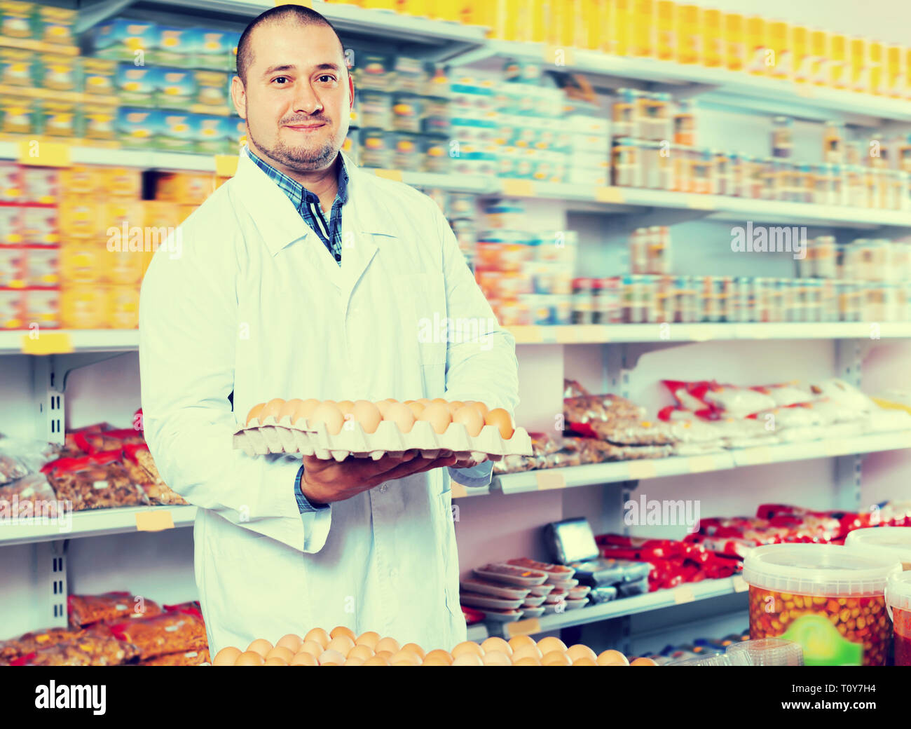 Happy salesman offering chicken eggs in ordinary food shop Stock Photo ...