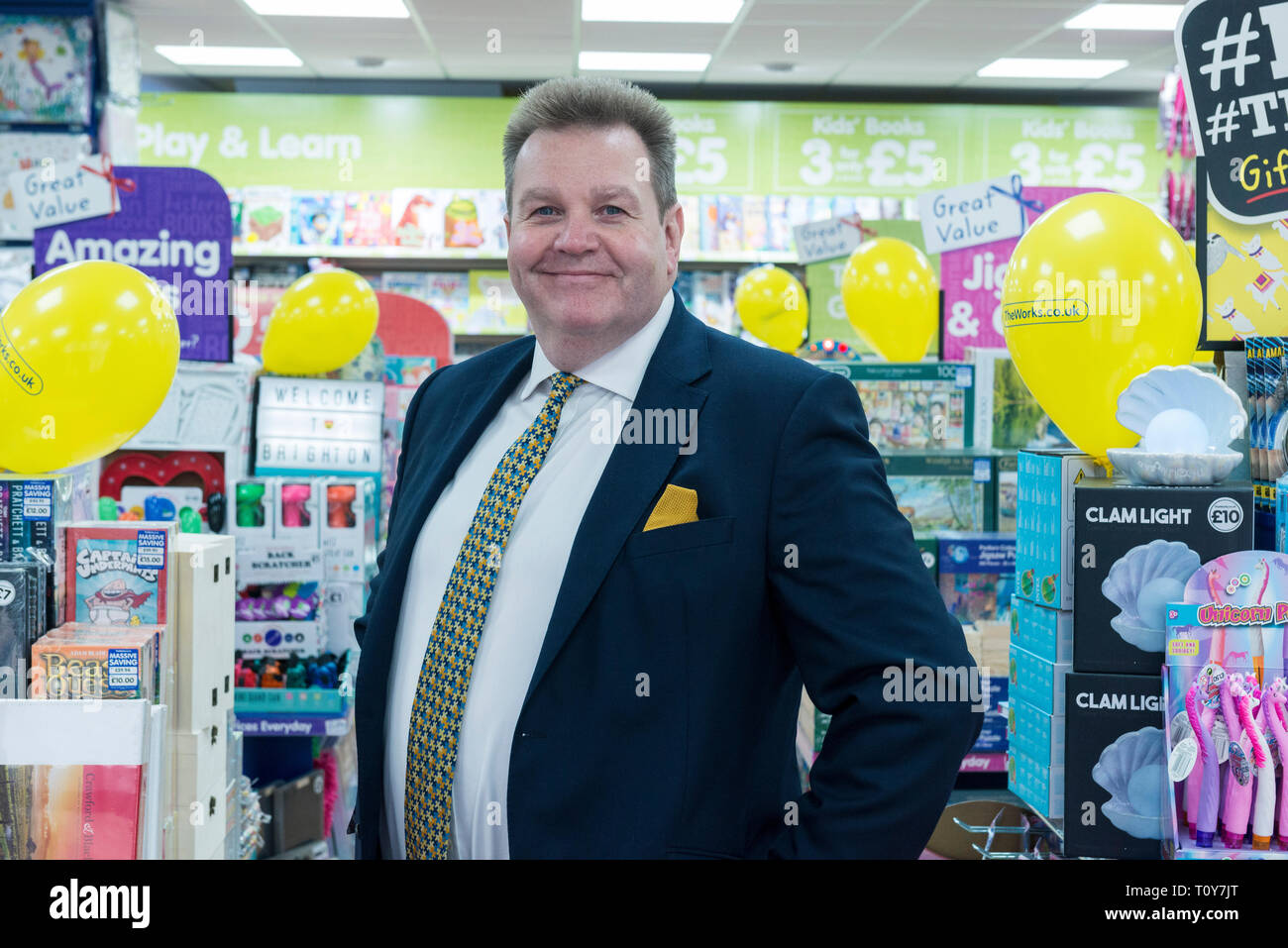 The CEO / Boss / manager of The Works stands in the store with products ...