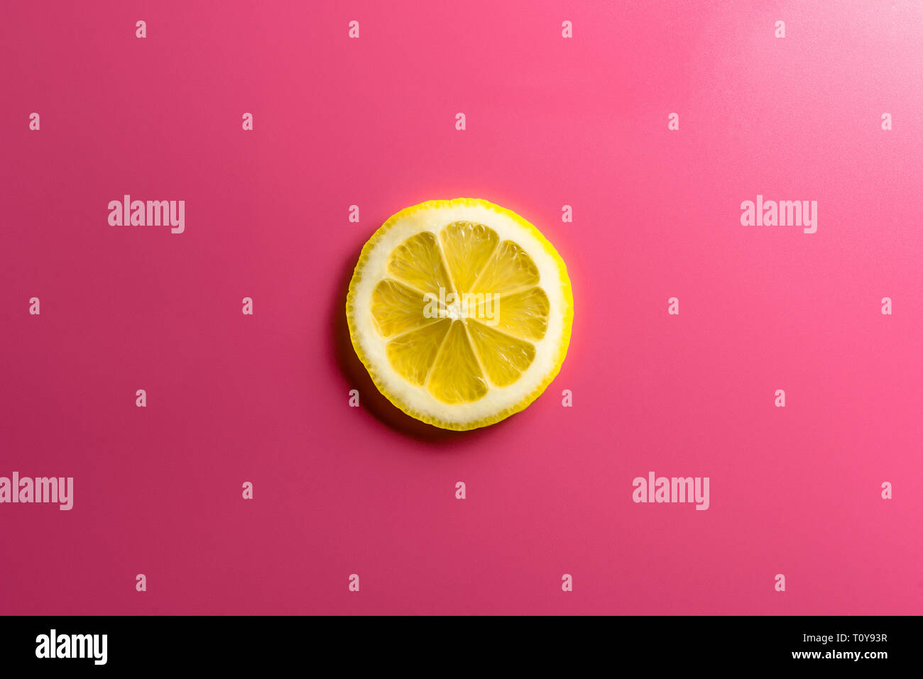 A single slice of lemon isolated on a pink background, illuminated by a ...