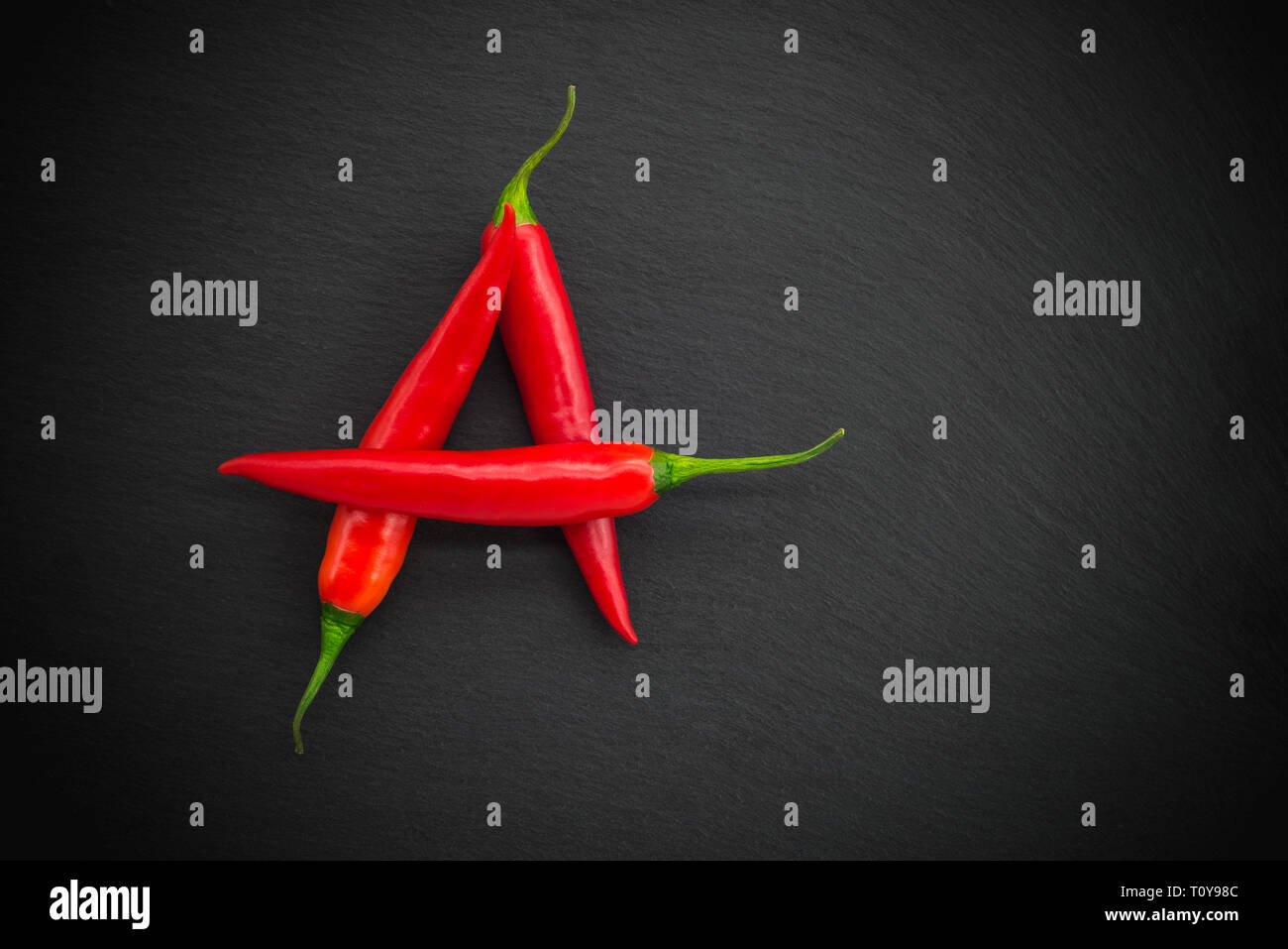 Letter A made of red hot chili peppers, on a dark slate background with ...