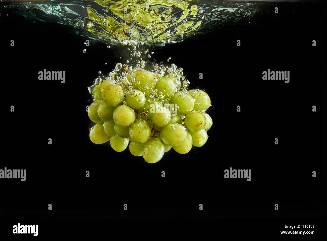 Fresh green grapes bunch splashing into water. Isolated on black ...