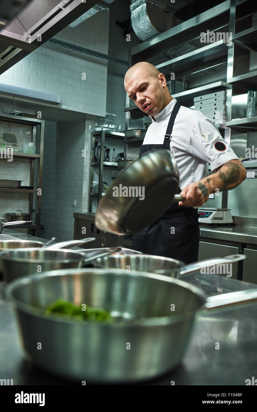 Very hot. Vertical photo of concentrated chef in apron with several ...