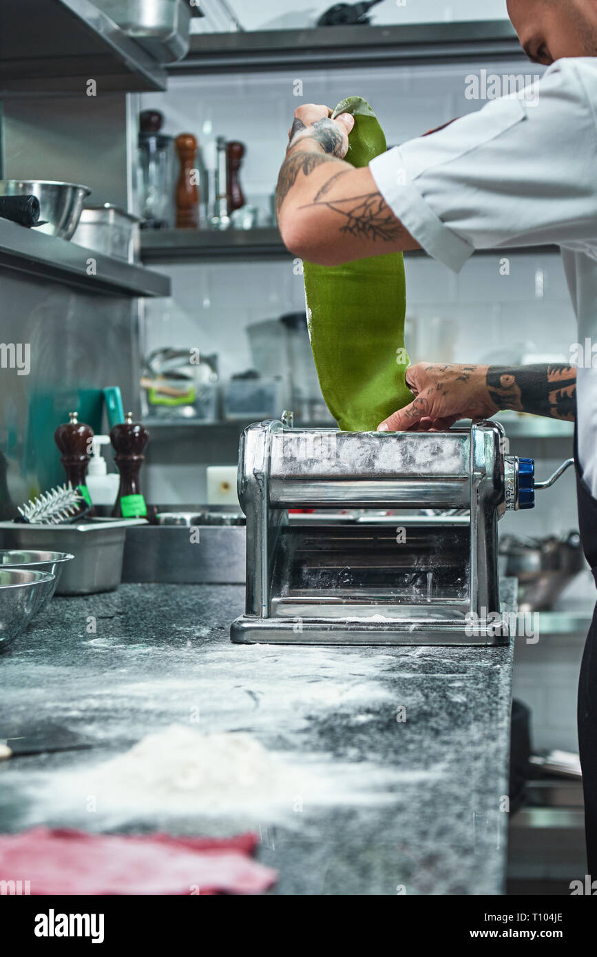 Making italian pasta. Cropped image of male chef rolling a green dough ...