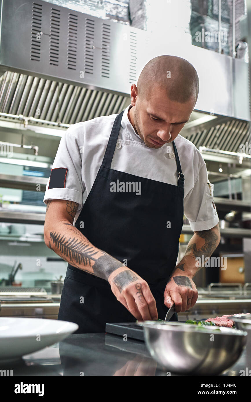 Preparing a salad. Handsome chef with tattoos on his arms cutting ...